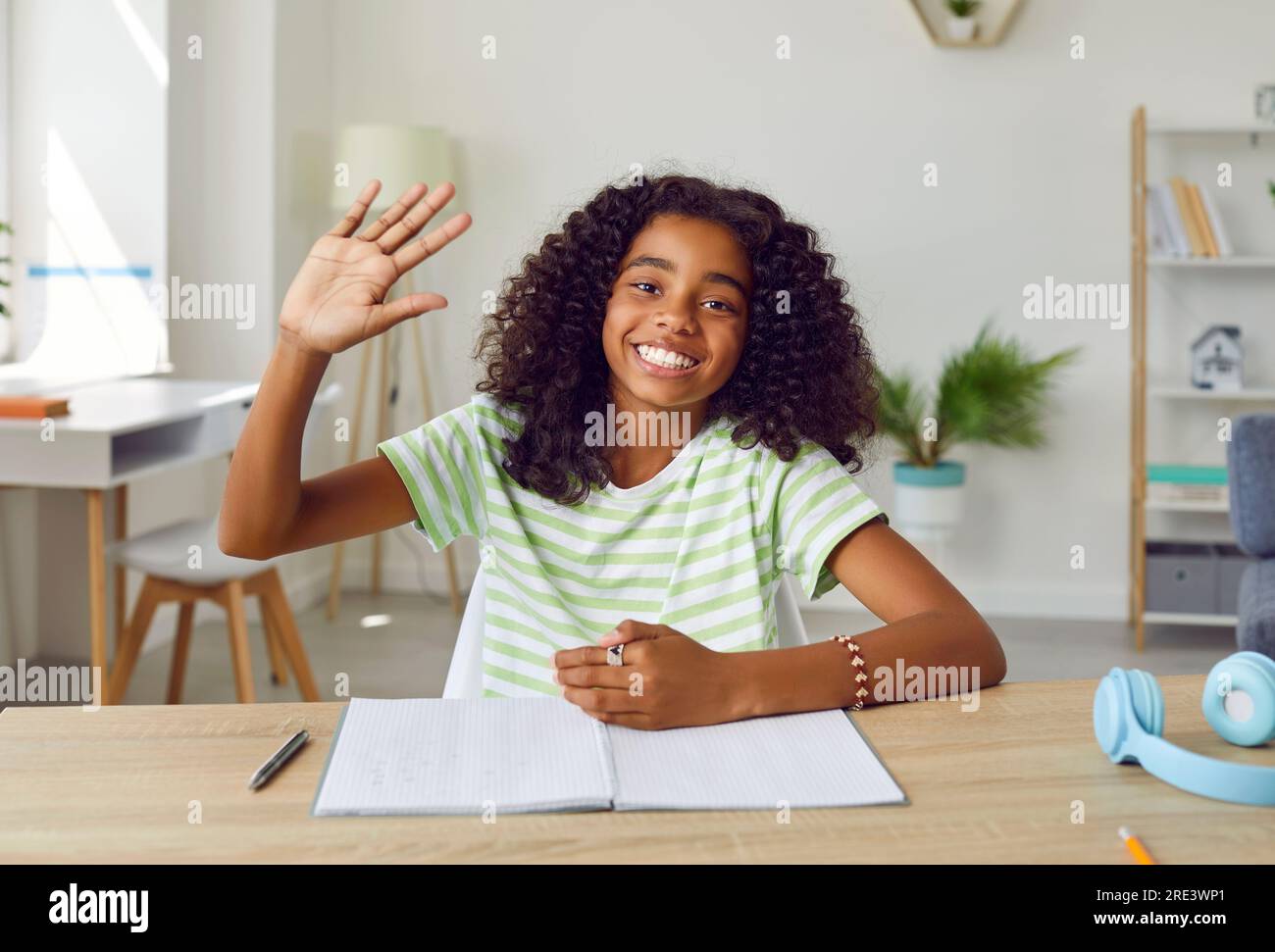 African american smiling girl waving her hand looking at camera sitting ...