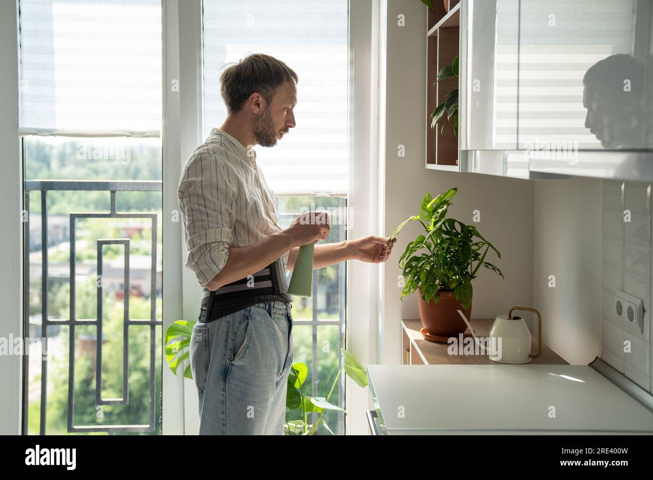 Man in sick leave taking care houseplants at home on kitchen wearing ...