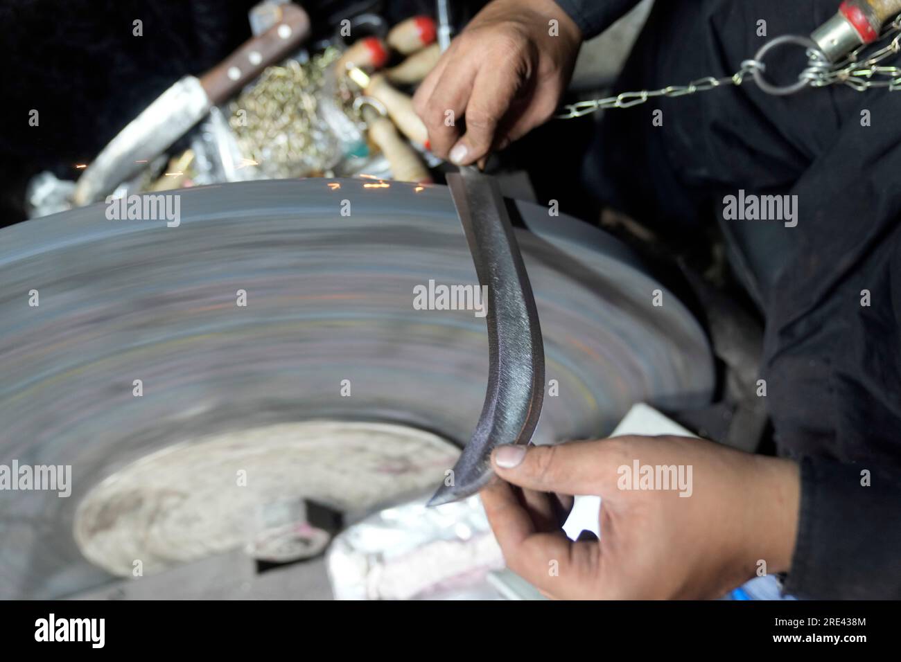 A Pakistani iron smith sharpens knives, as bunches of knives and chains ...