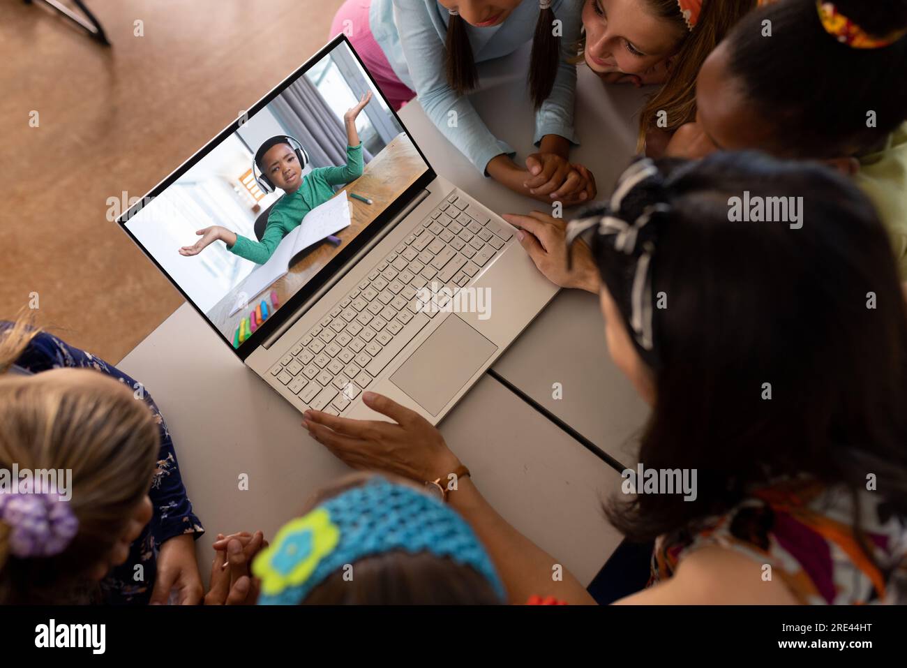 Multiracial teacher and students looking at boy on laptop screen while ...