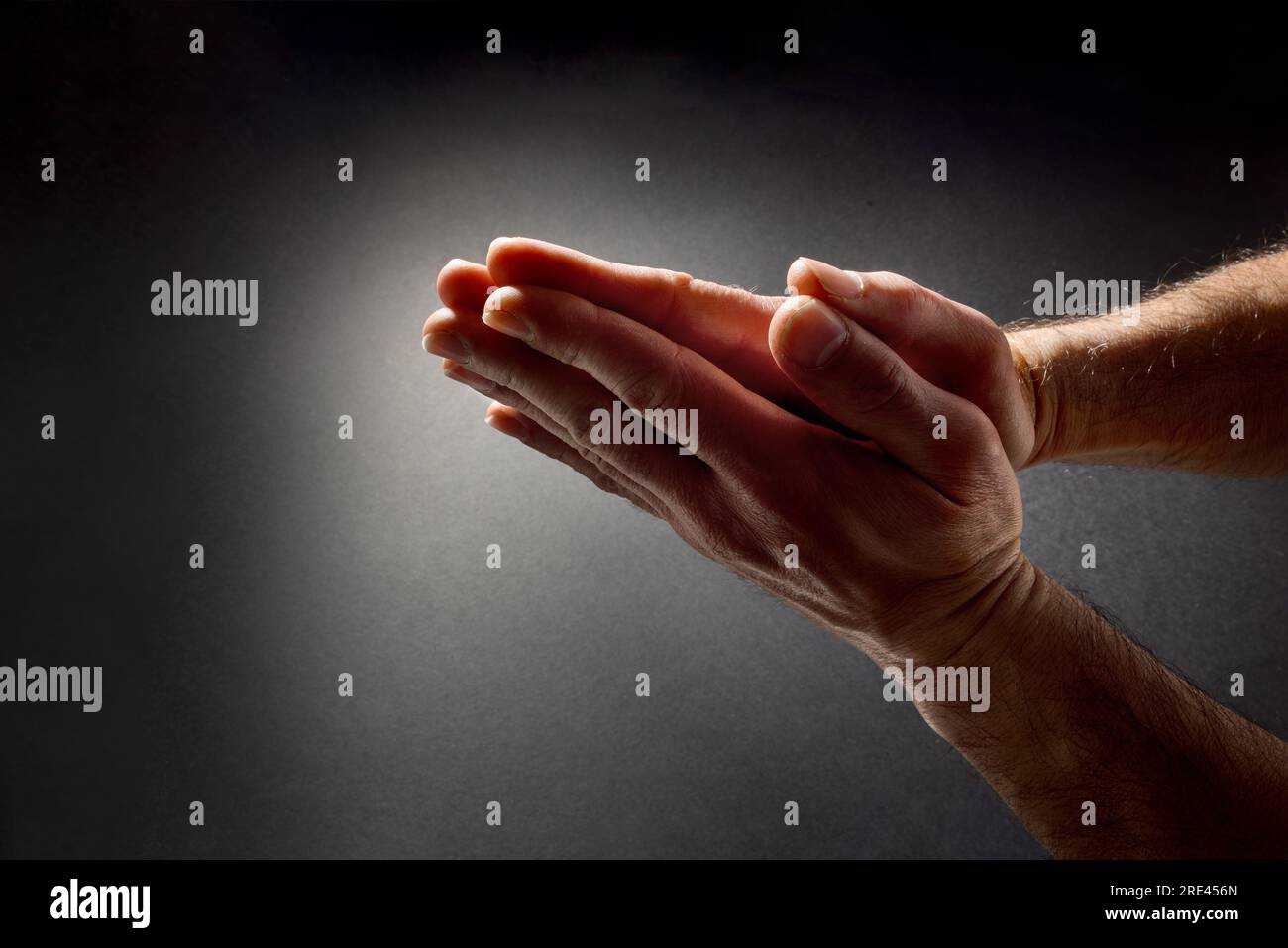 Praying man with hands with palms together contrasted with beam of ...