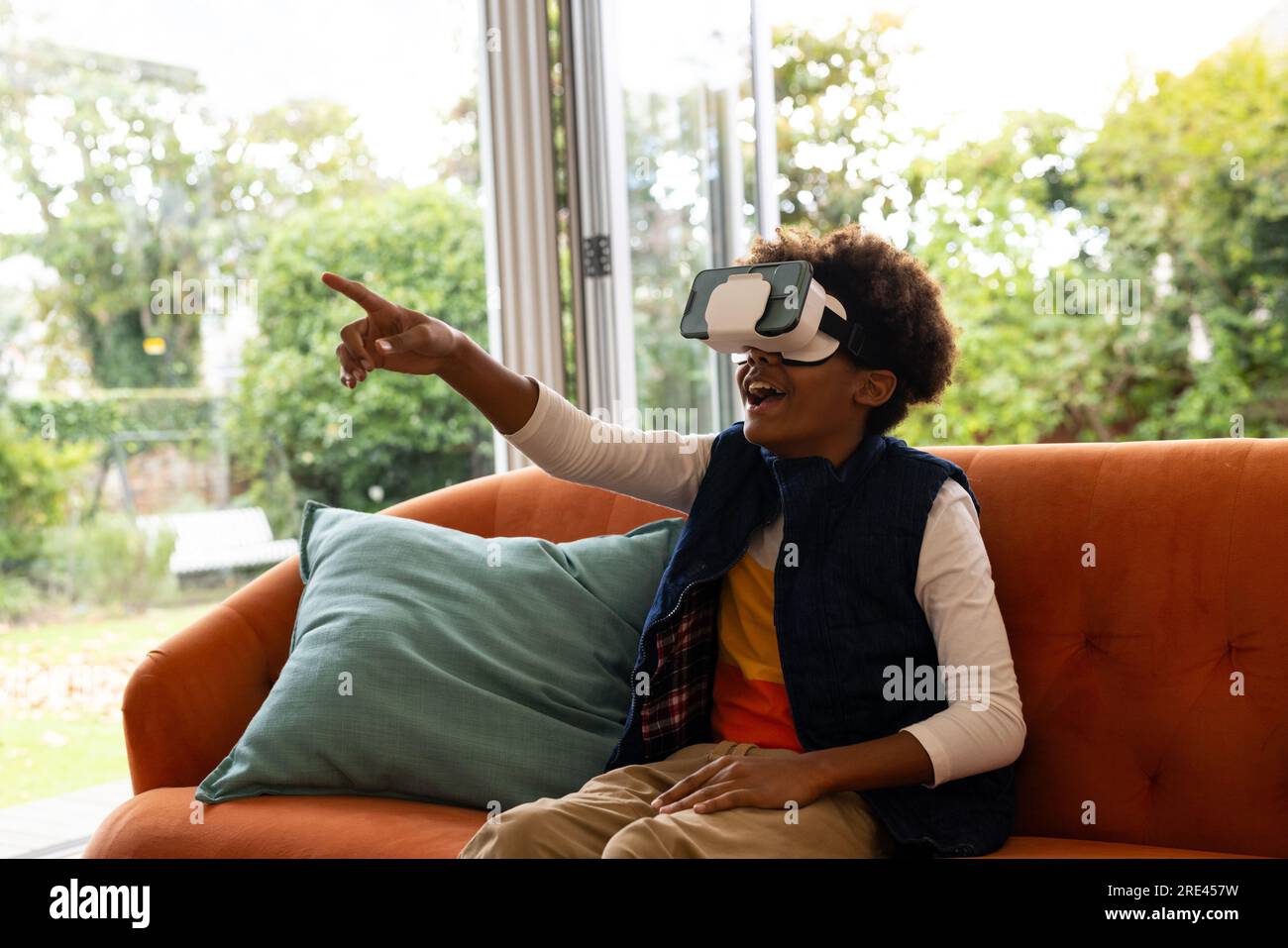 Happy african american boy sitting on sofa using vr headset and ...
