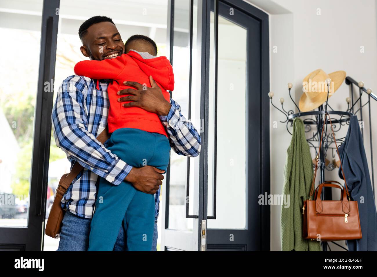 Happy African American Father Holding Son In Front Door At Home Stock