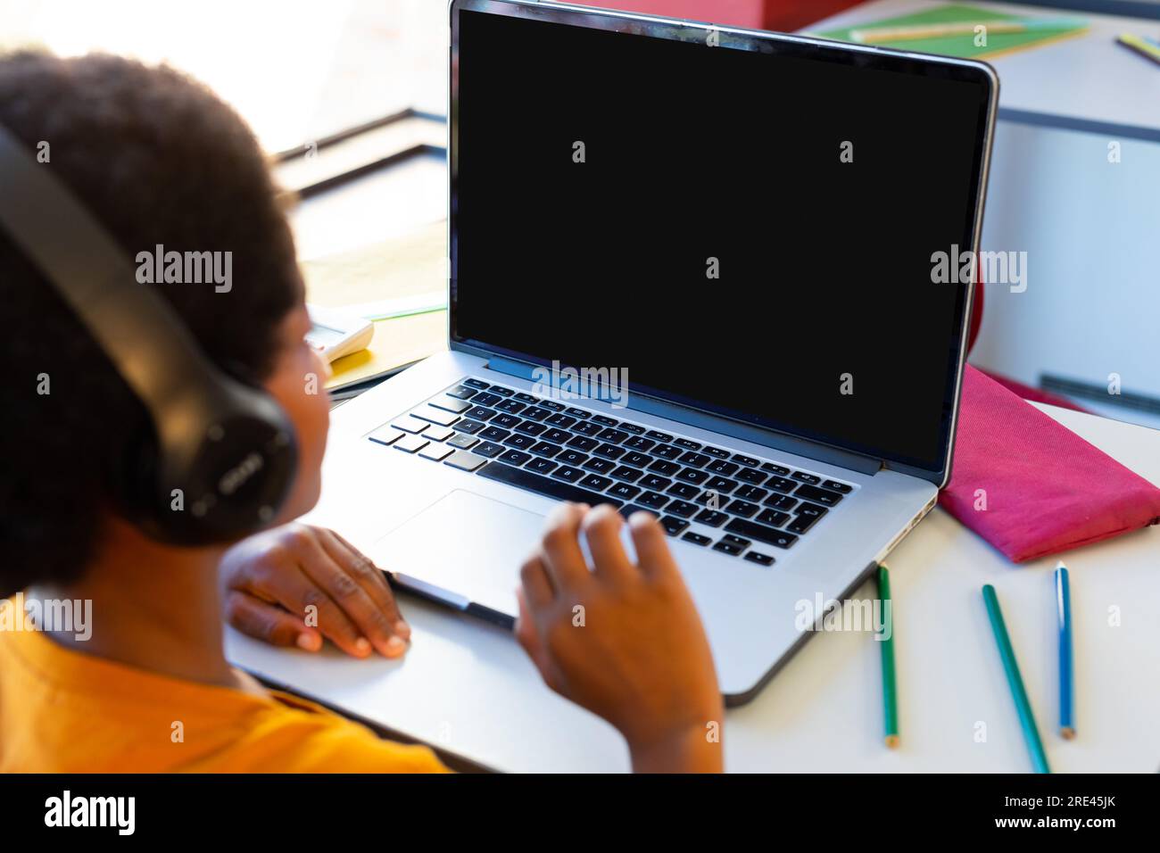 Rear view of a biracial boy wearing headphones having a video call on laptop with copy space at ...
