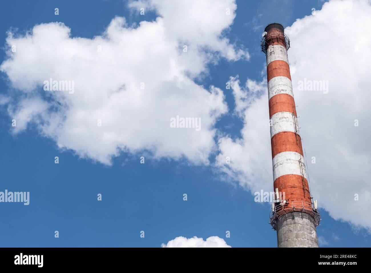 A high red-white chimney of a boiler room against a blue sky clouds ...