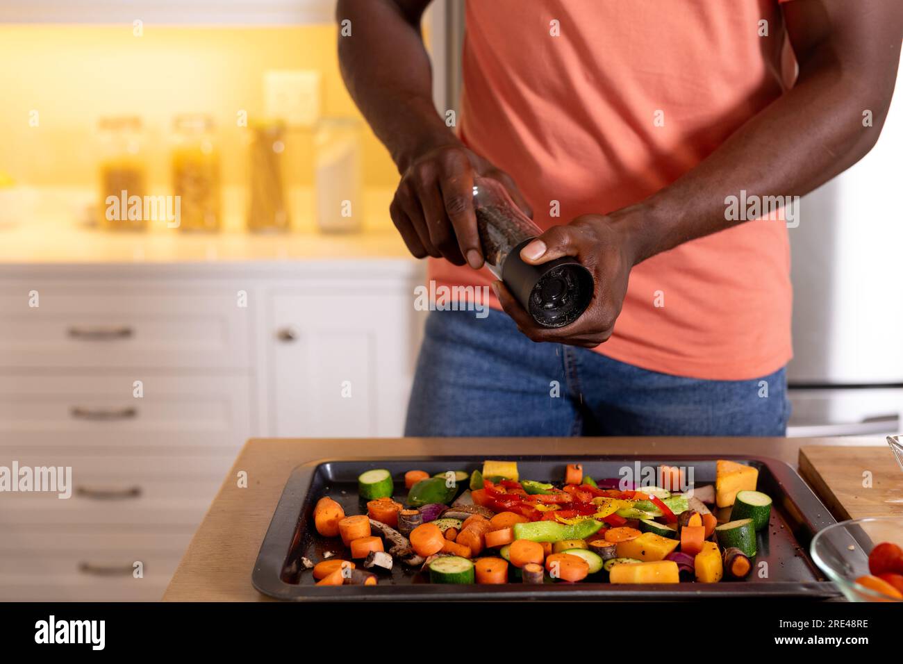 Midsection of african american man seasoning vegetables in kitchen ...