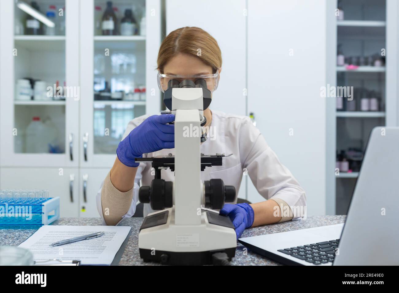 Serious and focused female researcher working with microscope inside laboratory, mature and ...