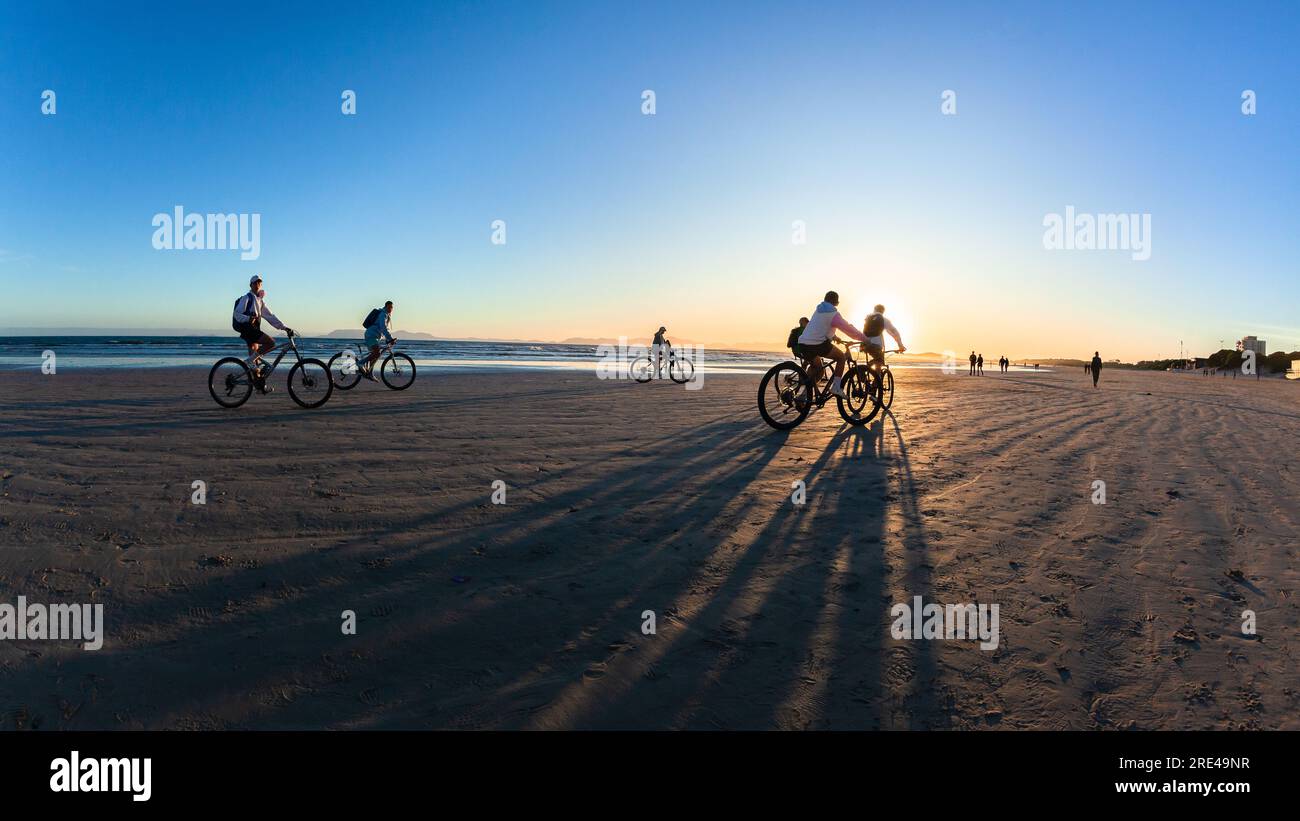 Beach ocean coastline with riders bicycles cycling silhouettes as sun ...