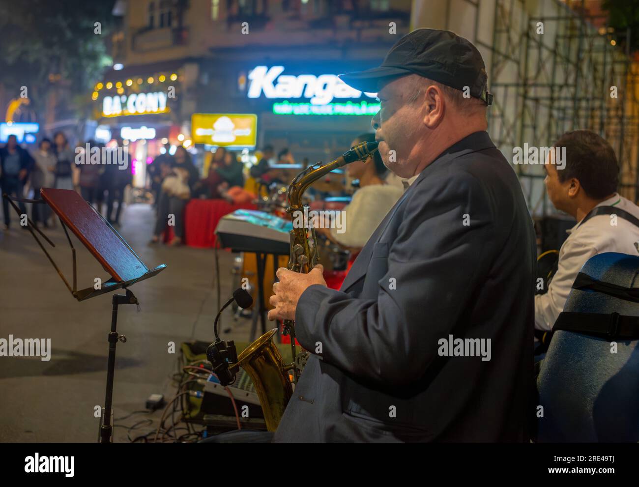 A Vietnamese man plays saxophone in a band in the street at night in ...