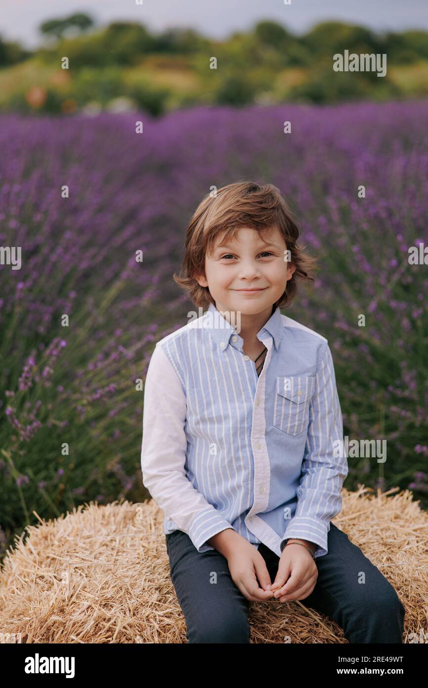 Joyful child boy sitting on hay bale against background of blooming ...