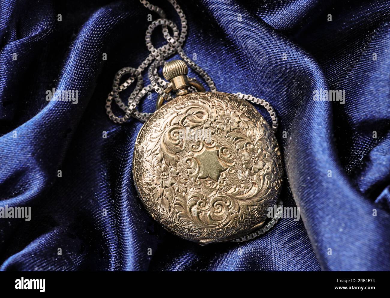A gold fob watch on a silken blue background, the rear with floral ...