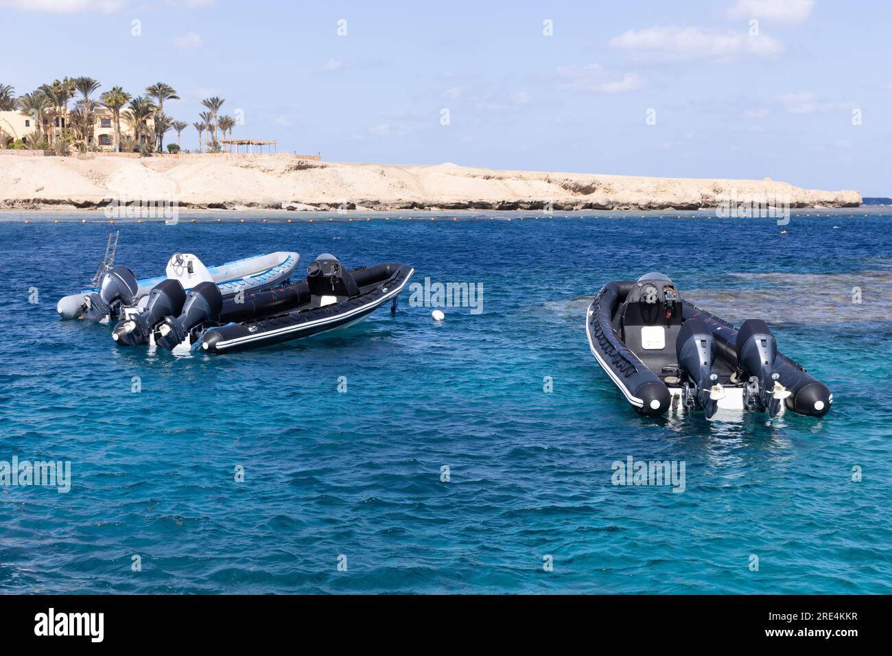 Three inflatable boats sit empty at anchor on a coral reef with crystal ...