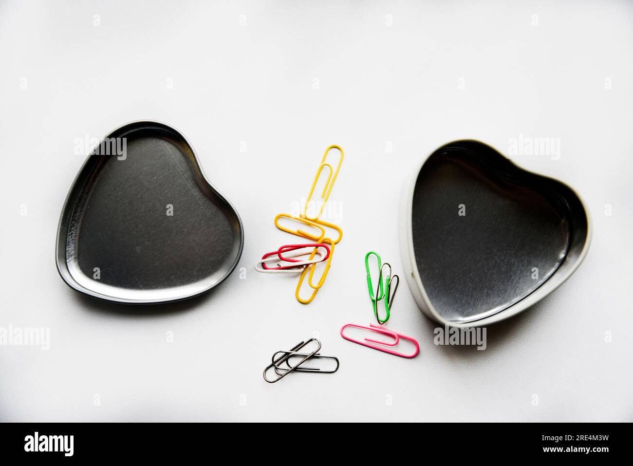 Colored paper clips and a tin box in the shape of a heart on a white ...