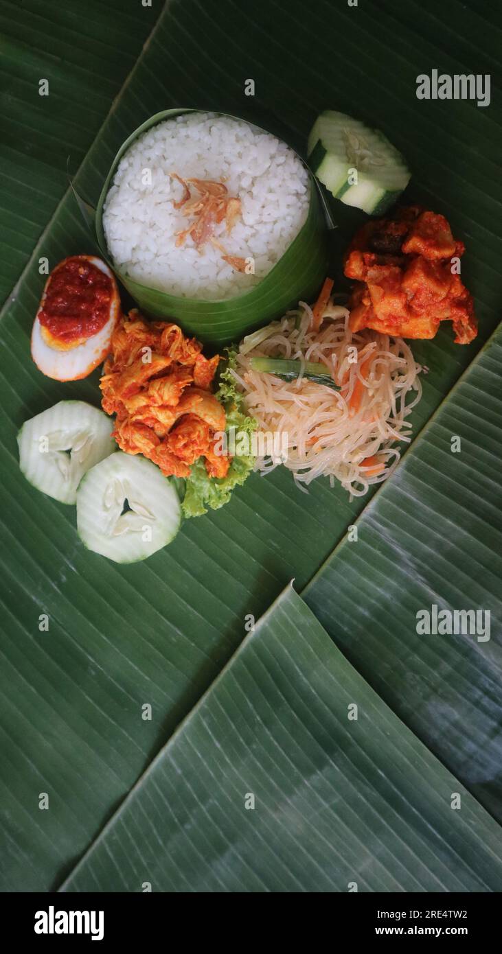 Savory rice, noodles, cucumber, and seasoned potatoes on a banana leaf ...