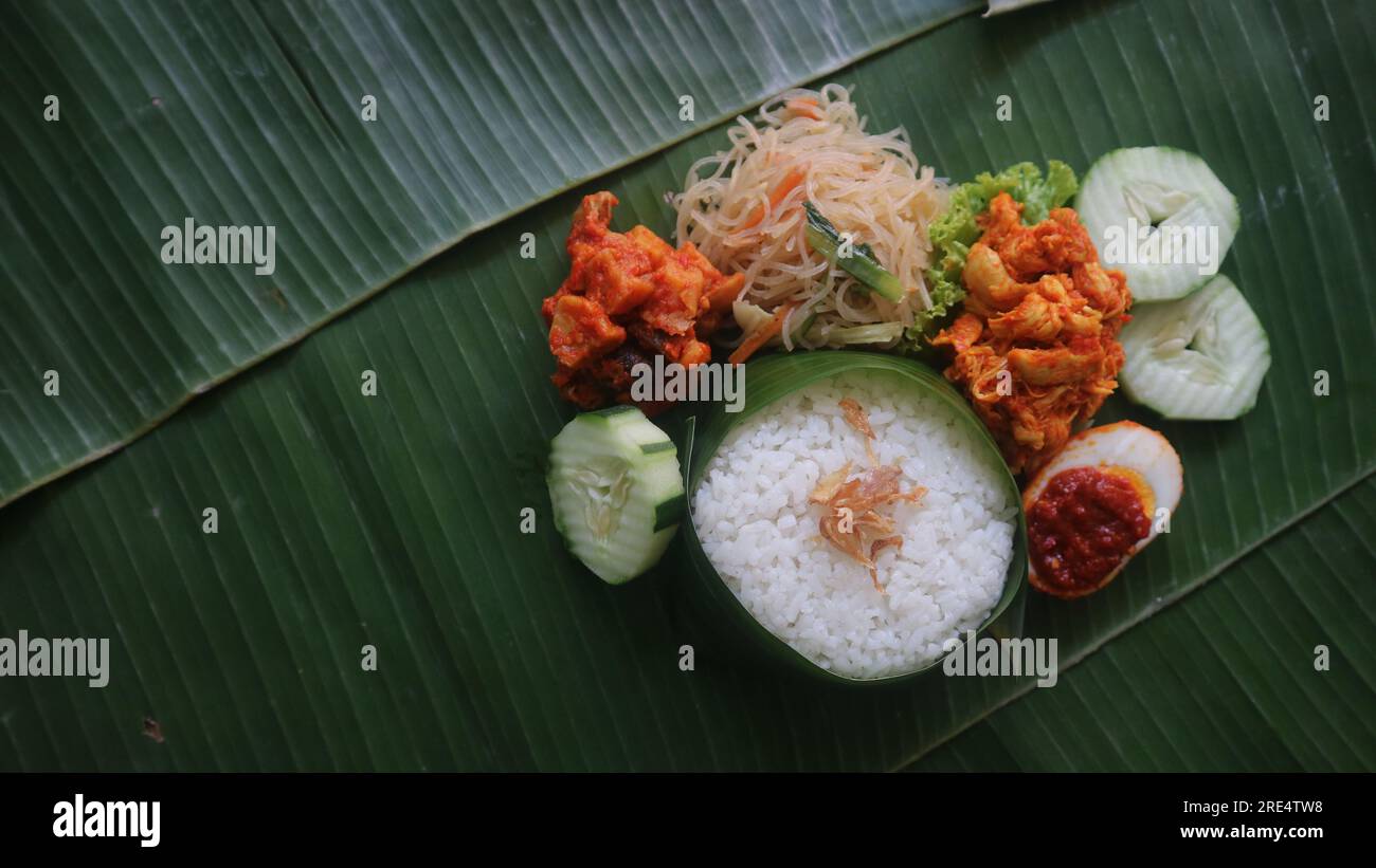 Savory rice, noodles, cucumber, and seasoned potatoes on a banana leaf ...