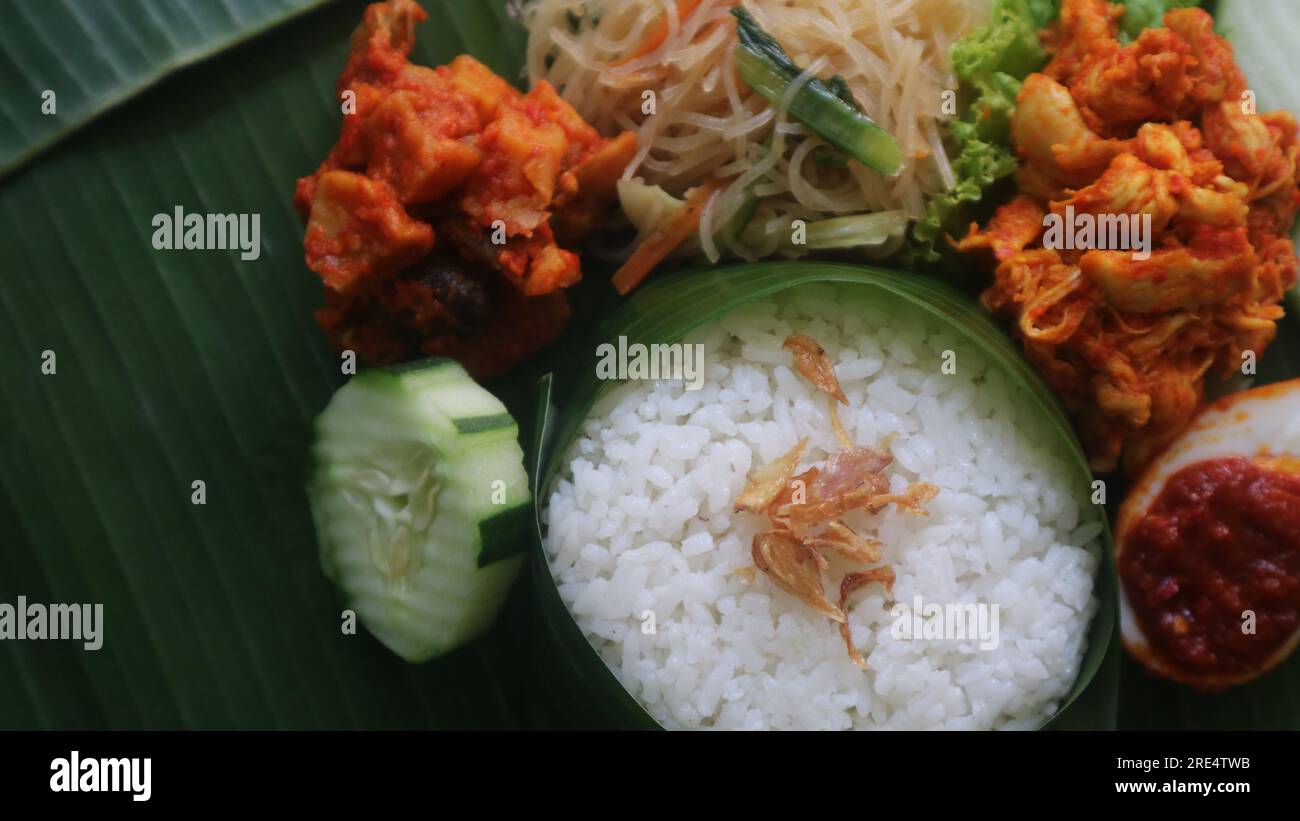 Savory rice, noodles, cucumber, and seasoned potatoes on a banana leaf ...