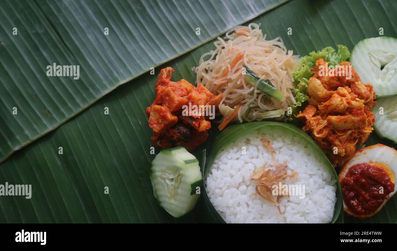 Savory rice, noodles, cucumber, and seasoned potatoes on a banana leaf ...