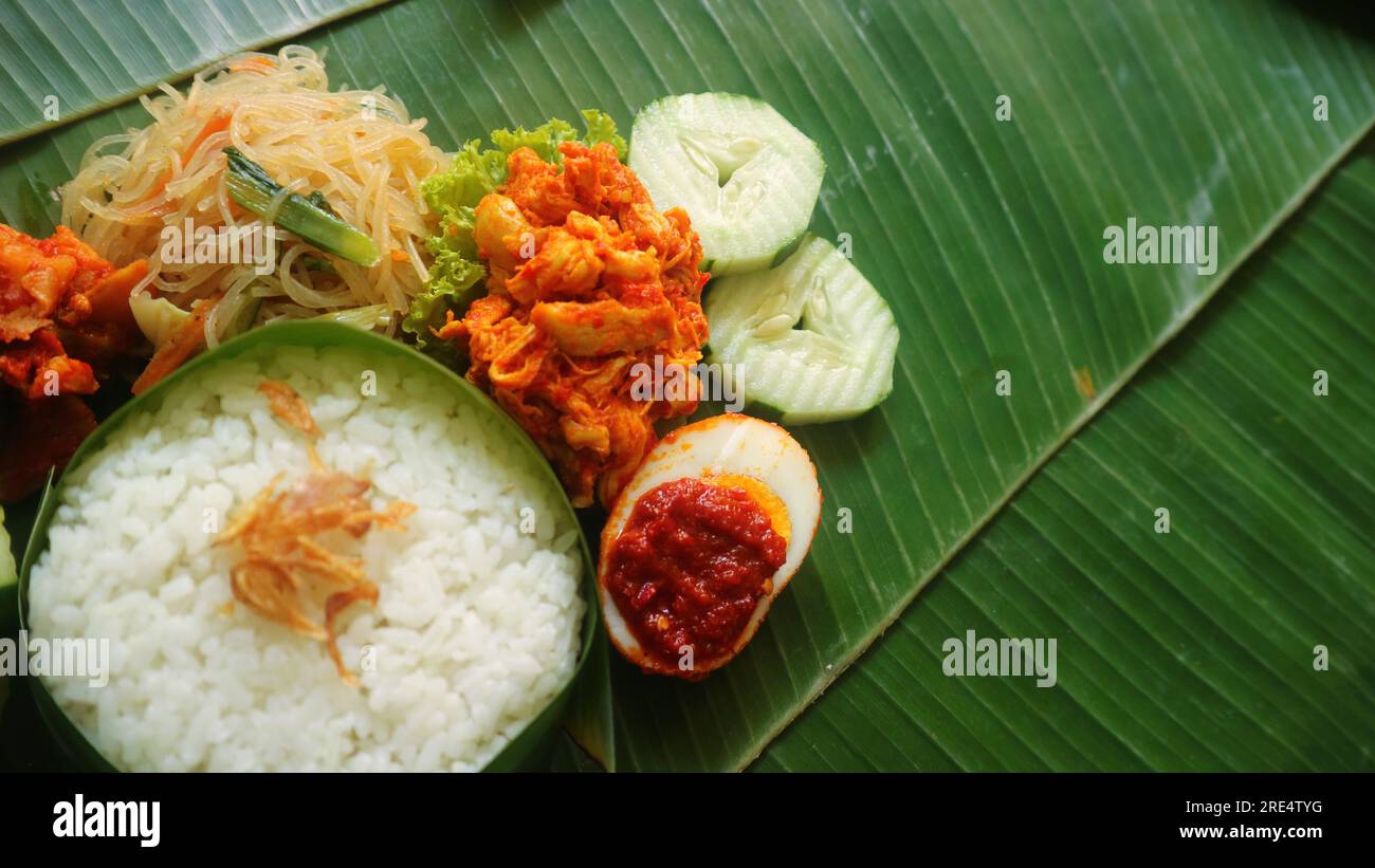 Savory rice, noodles, cucumber, and seasoned potatoes on a banana leaf ...