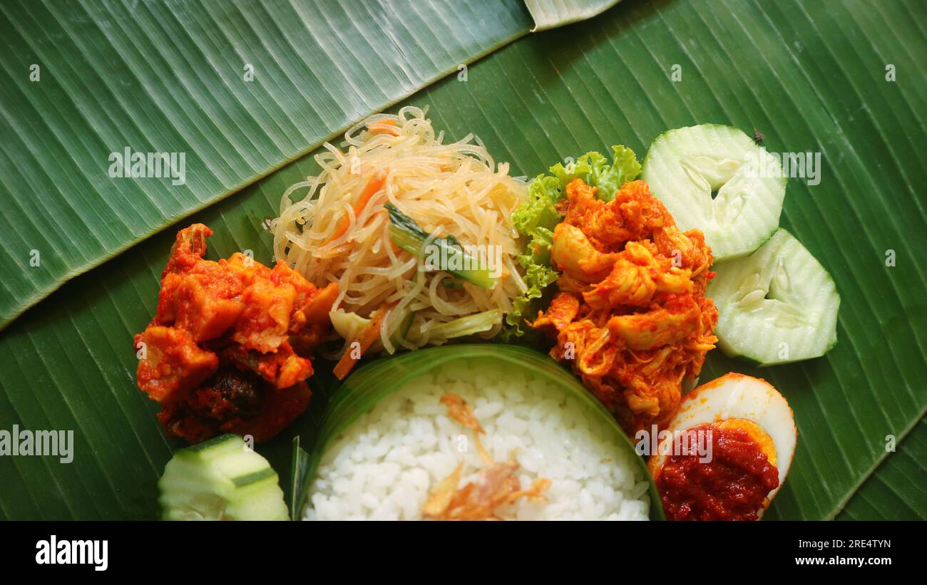 Savory rice, noodles, cucumber, and seasoned potatoes on a banana leaf ...