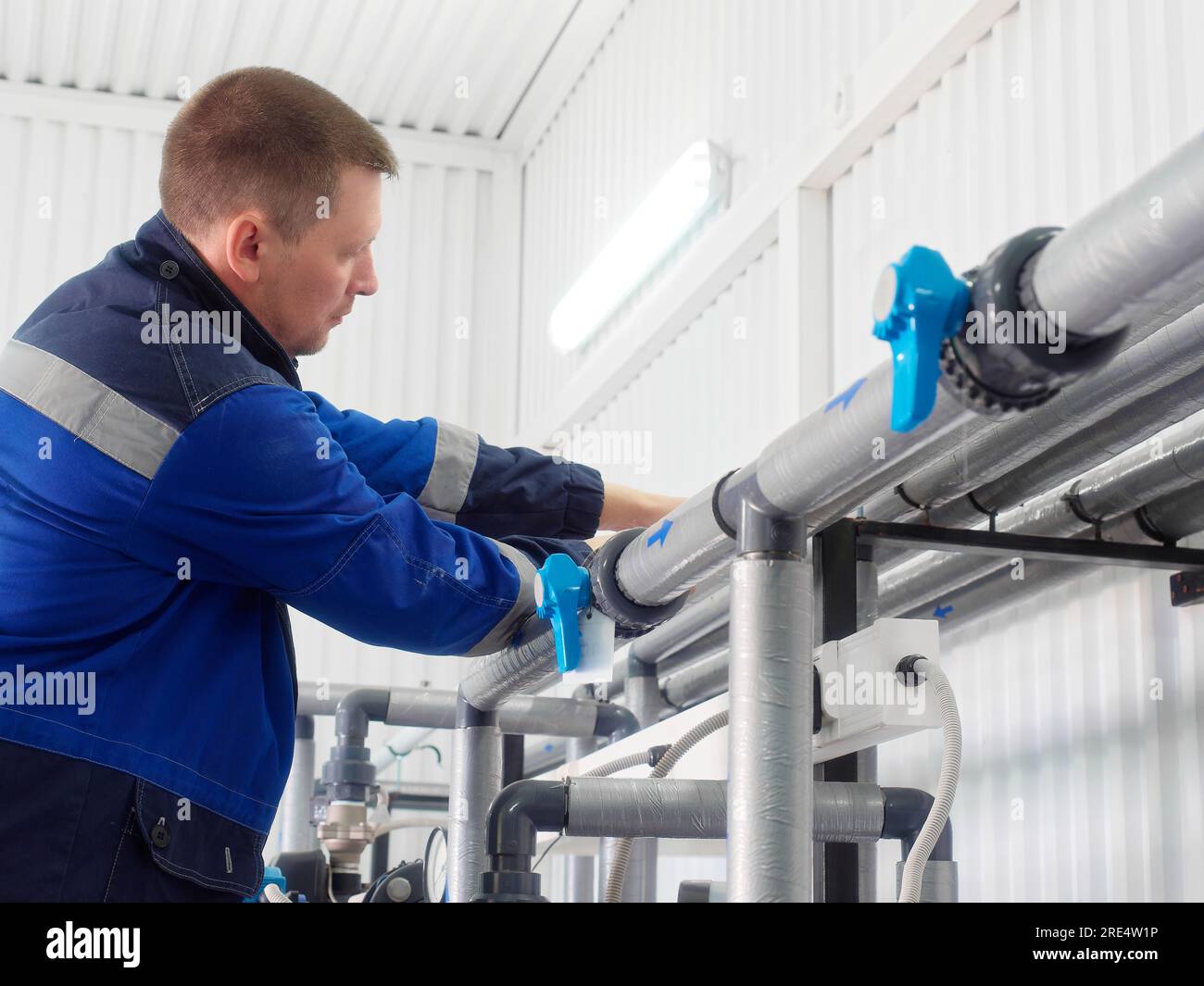 Plumber joins pipe coupling inside production facility. Worker repairs ...