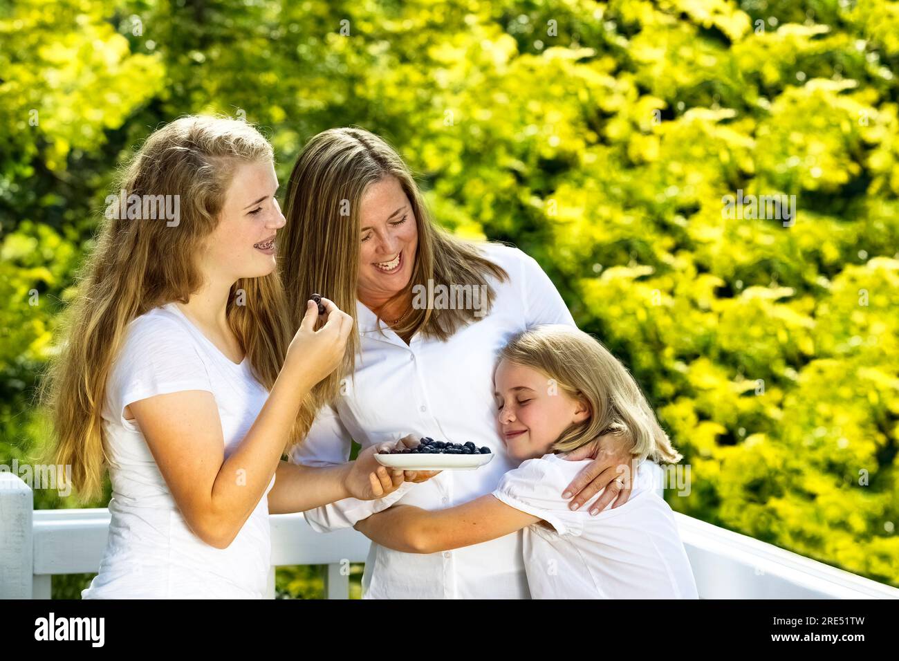 Mother and her daughters enjoying being outdoors while eating fresh blueberry fruit during a ...