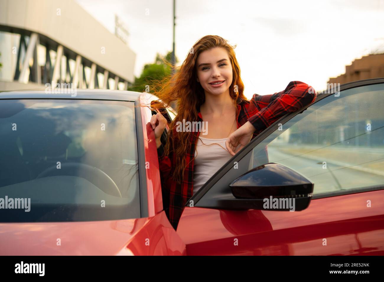With vibrant red hair, a young woman poses gracefully beside a gleaming ...
