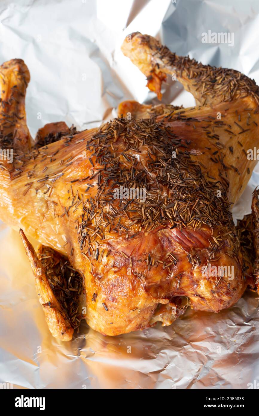 Whole roat chicken, covered in rosemary, on aluminium kitchen foil ...