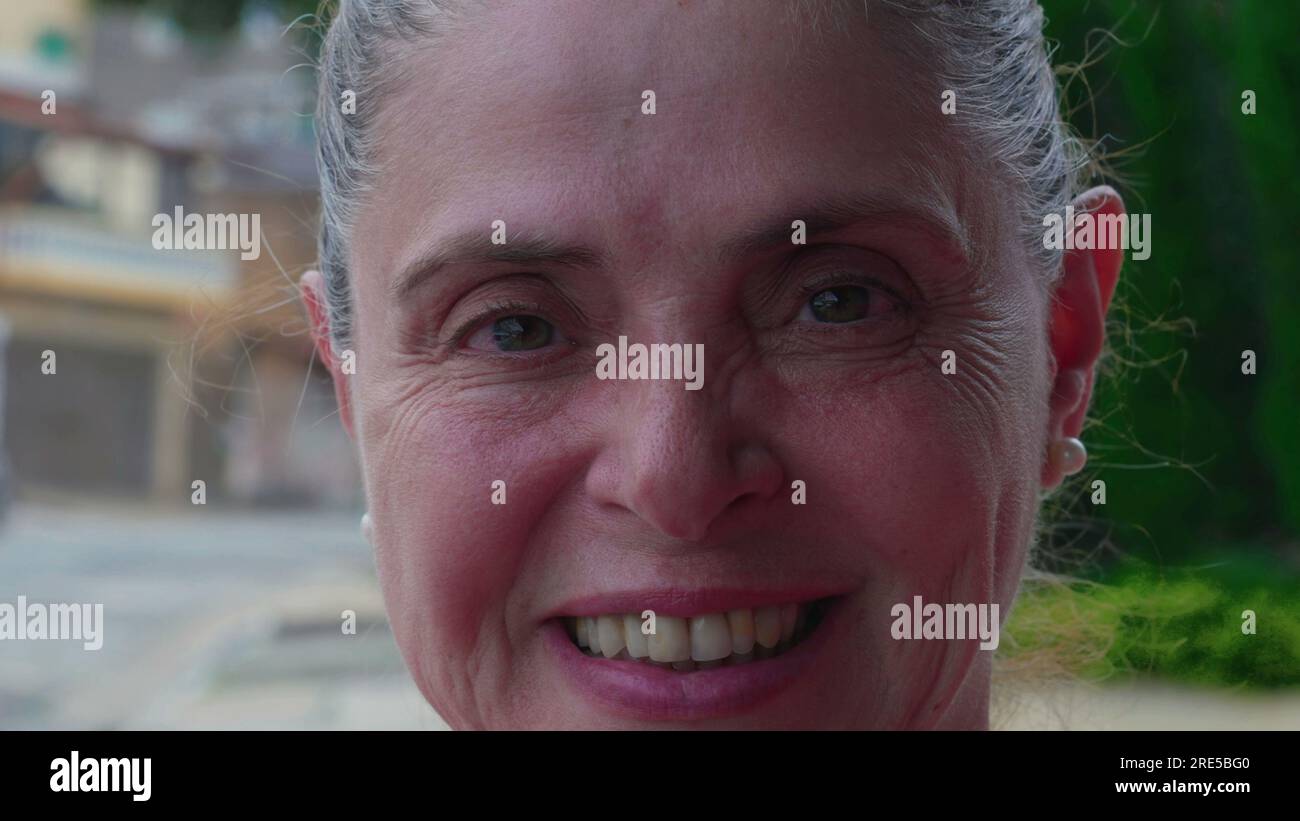 One joyful Brazilian mature woman in 50s smiling at camera standing ...