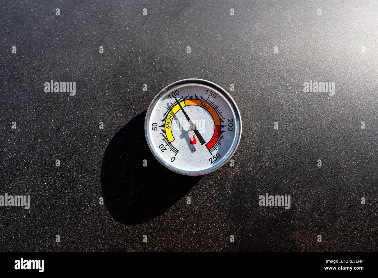 A round thermometer showing 100 degrees Celsius placed on a charcoal ...