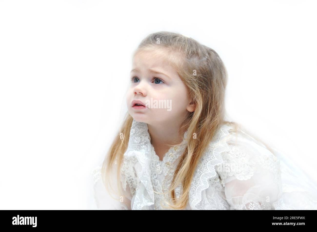 Little girl dressed in elegant and lacy gown looks upward with a ...
