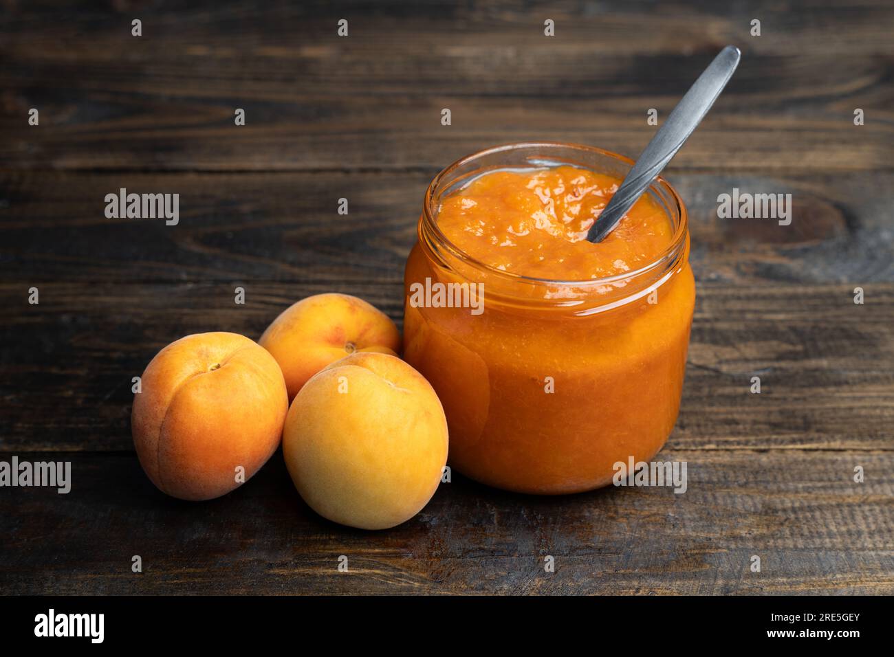Apricot jam in a glass jar with a spoon inside, fresh apricots on a ...