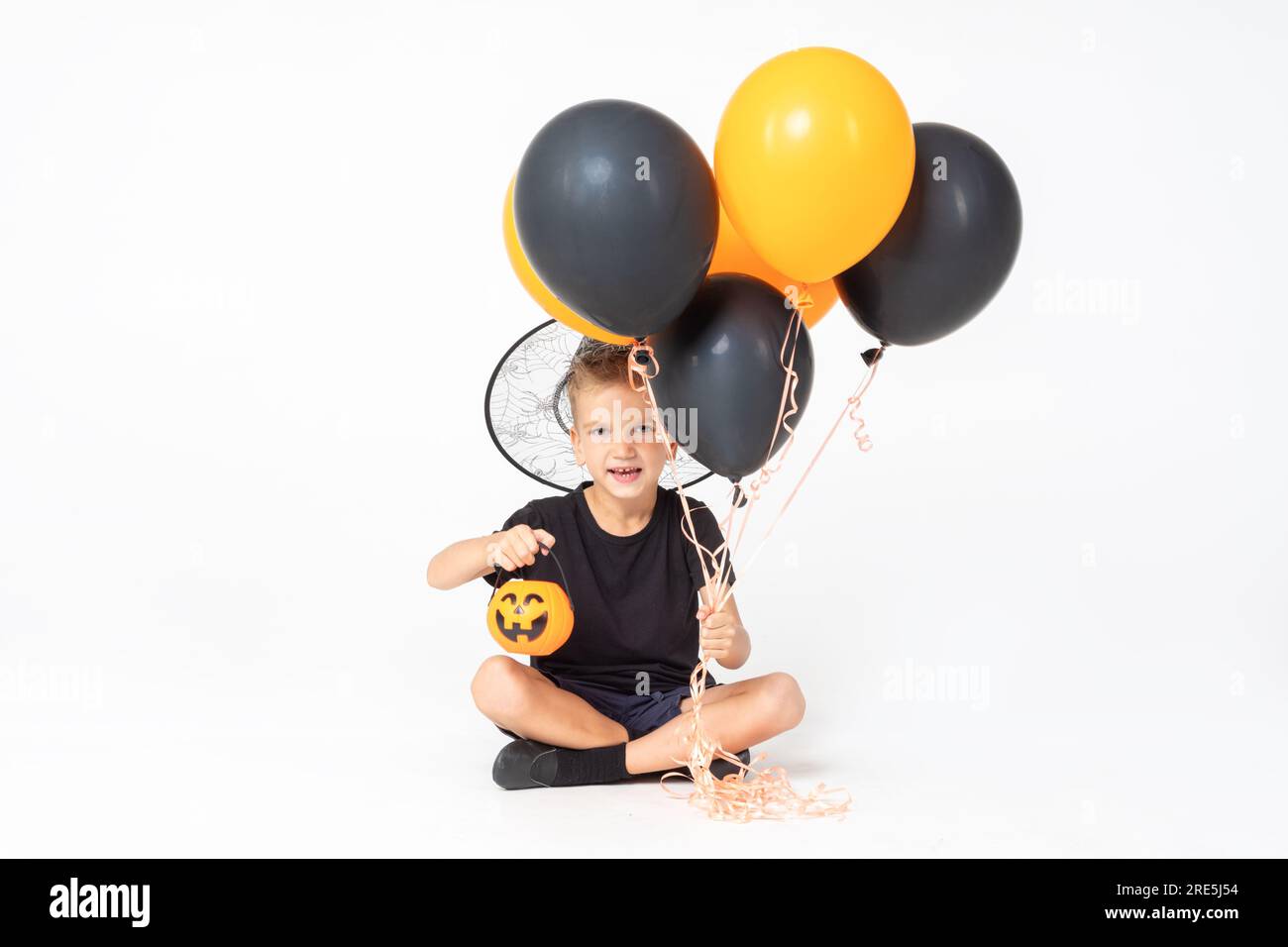 A cheerful happy boy in a wizard's hat holding a pumpkin-shaped bucket ...