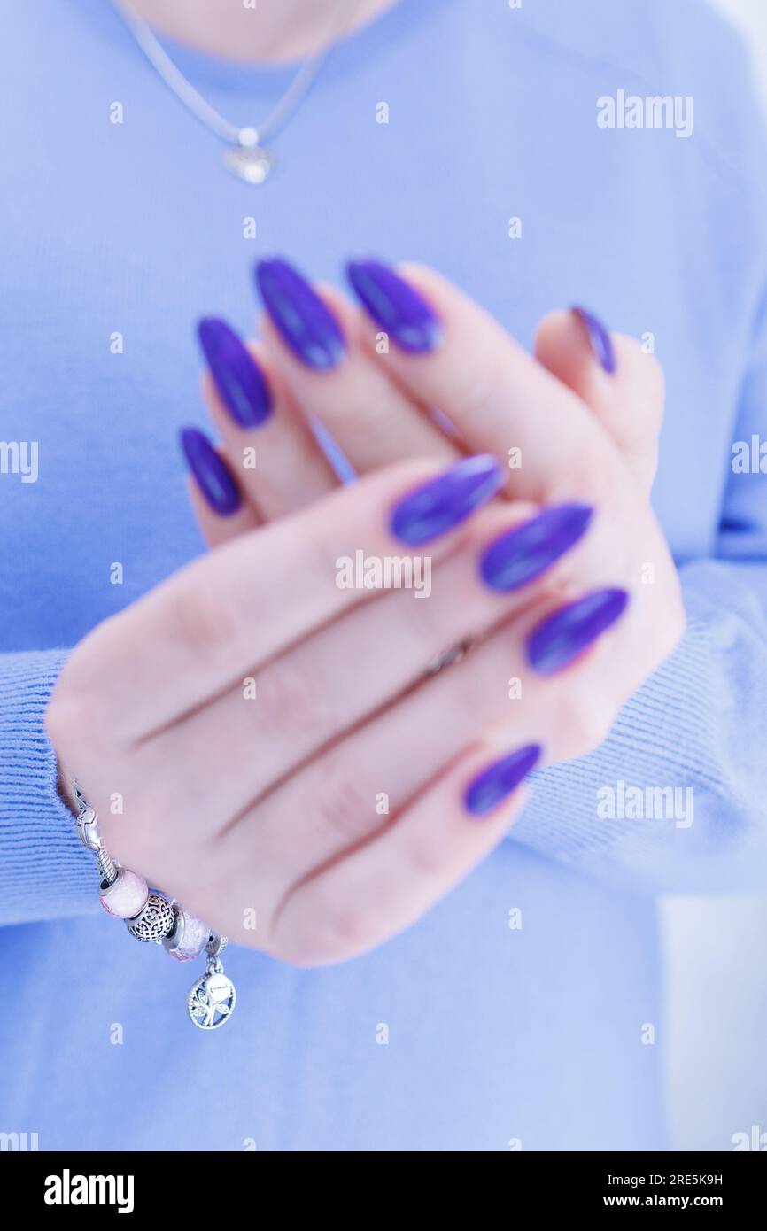 Female hand with long nails and a bottle of light blue lilac color nail ...