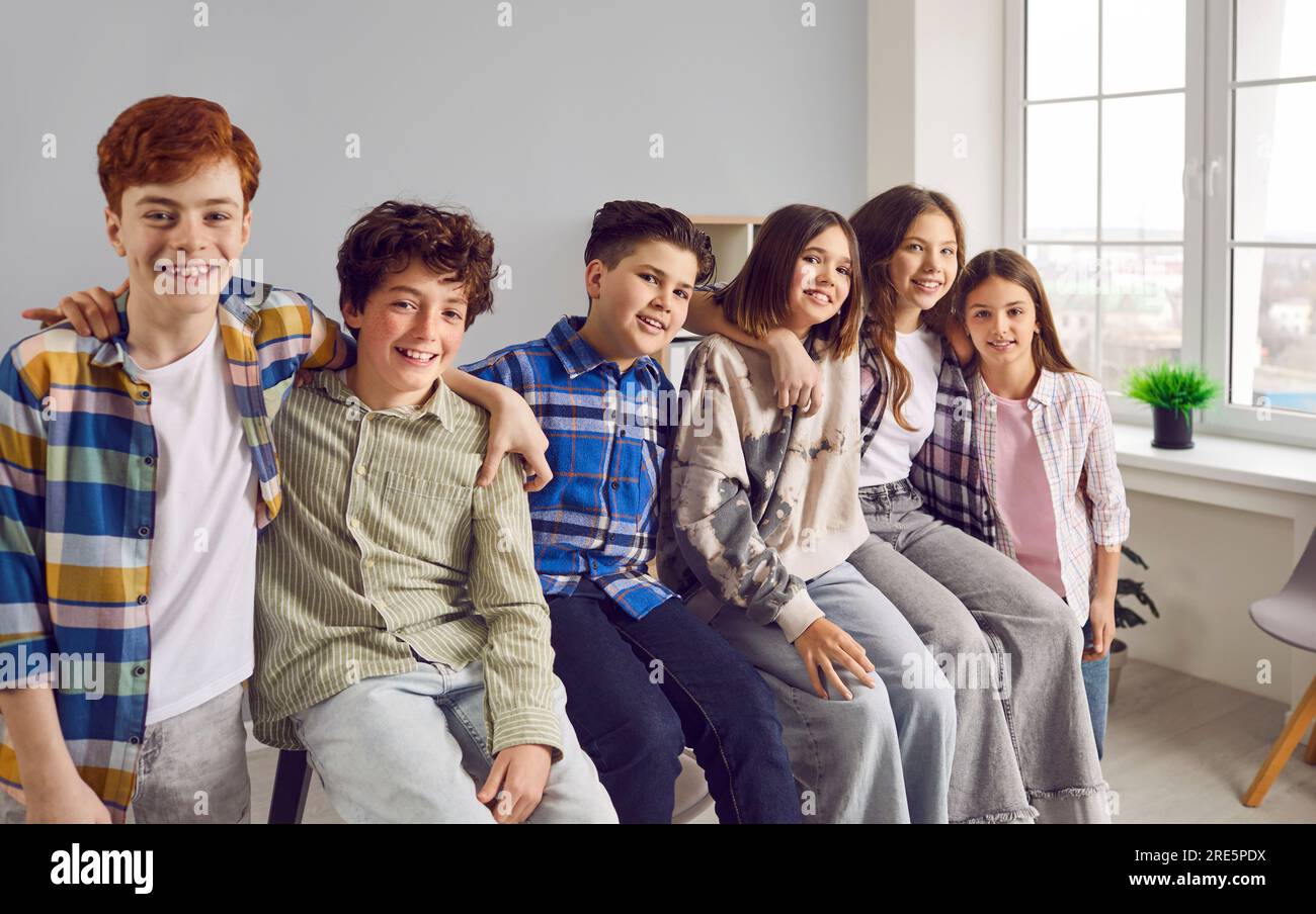 Happy school students sitting in row with their arms around each other ...