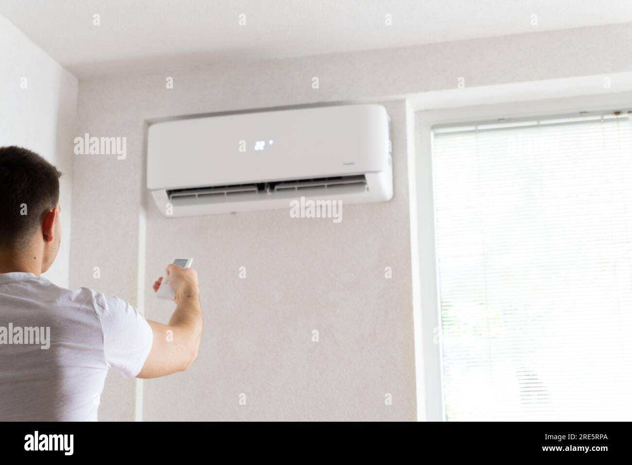 Young man switches air conditioning on. Handsome young man turning on ...