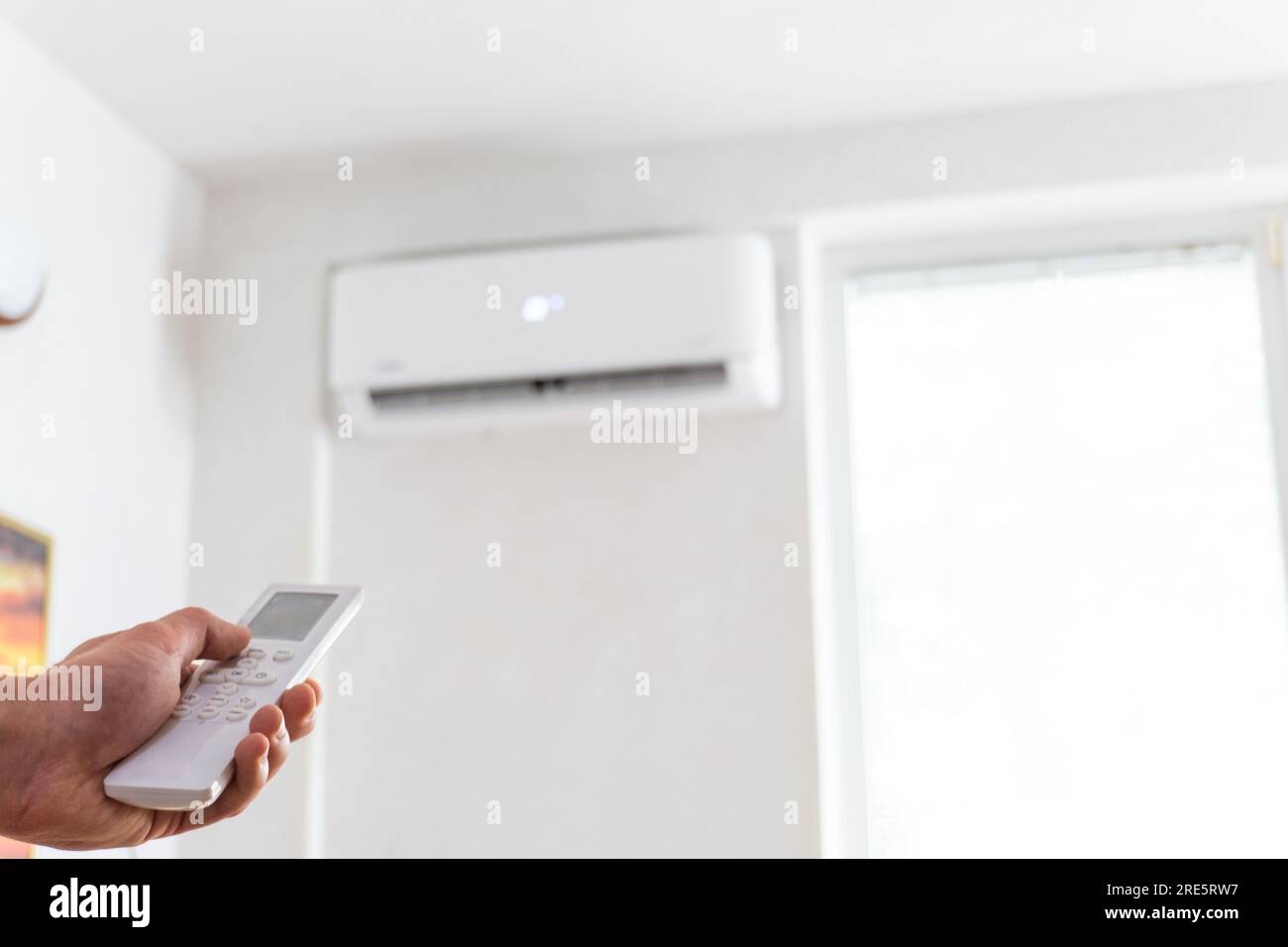 Hand holding remote control aimed at the air conditioner. Young man ...