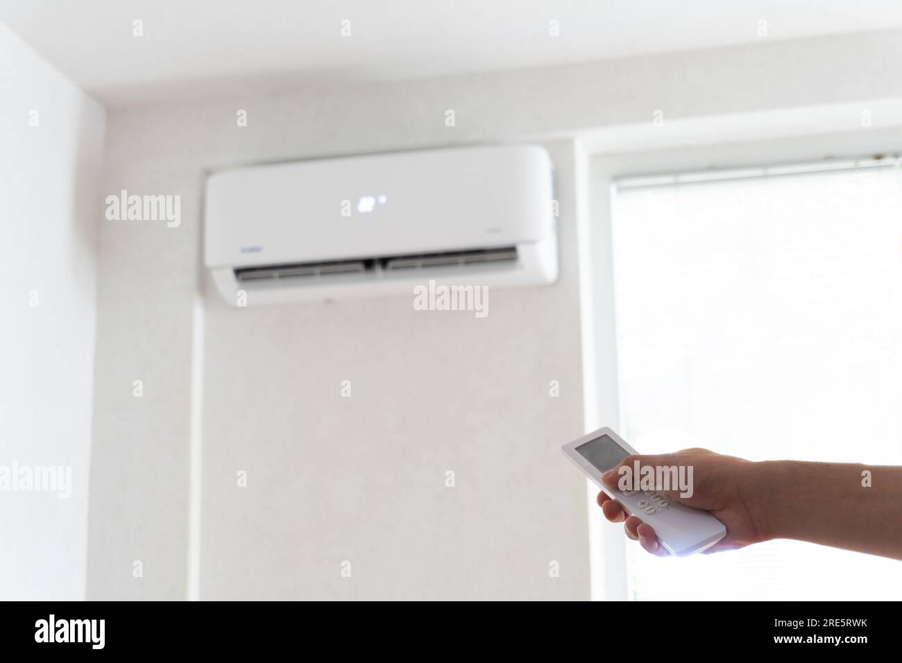 Hand holding remote control aimed at the air conditioner. Young man ...
