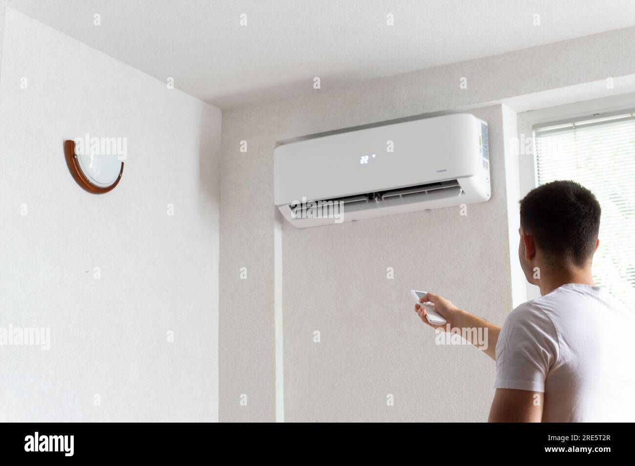 Young man switches air conditioning on. Handsome young man turning on ...