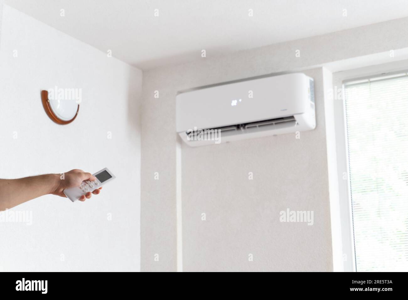 Hand holding remote control aimed at the air conditioner. Young man ...