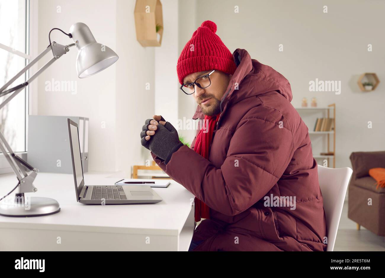 Man freezing indoors in a cold winter and trying to work on his laptop ...
