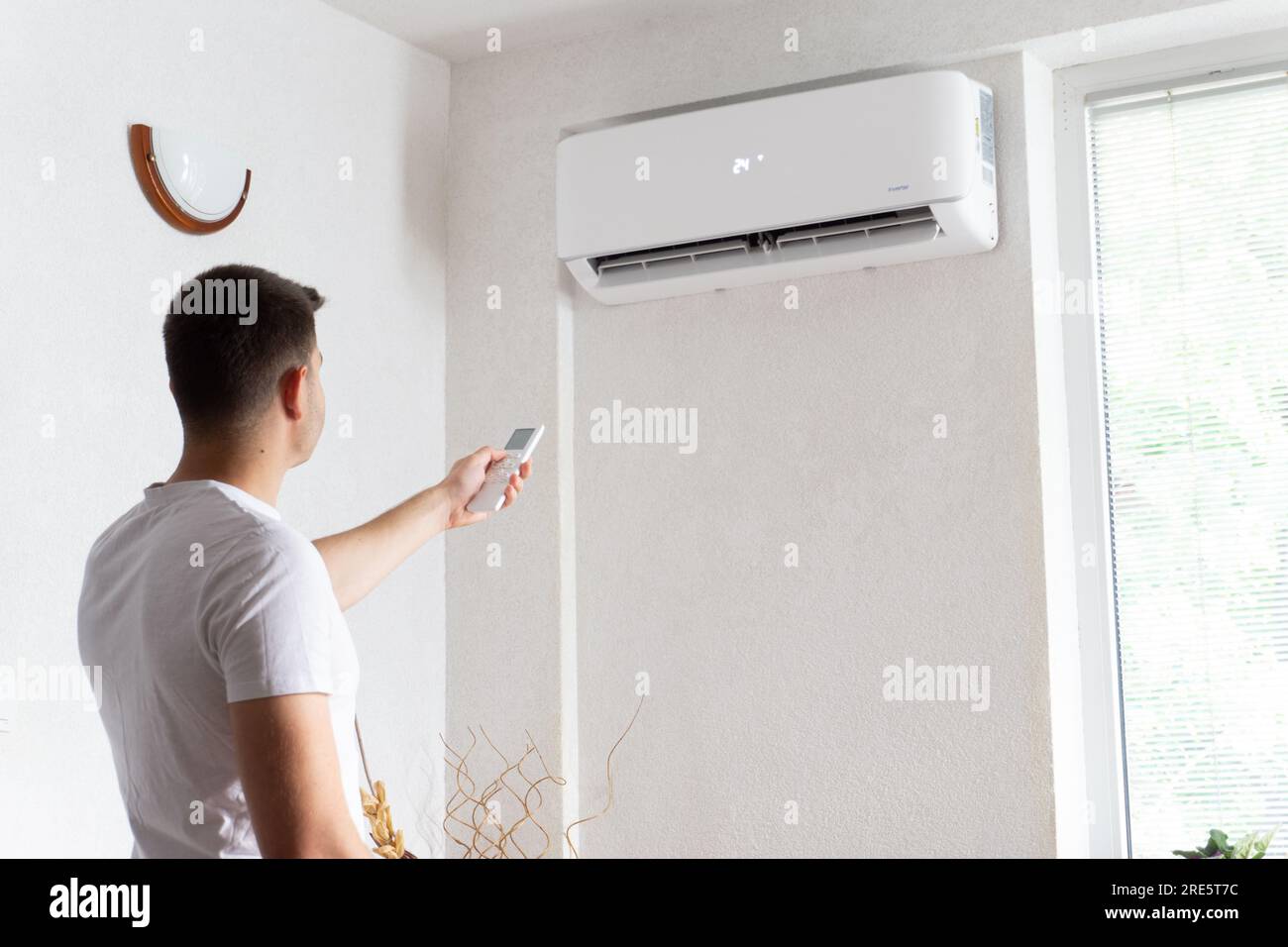 Young man switches air conditioning on. Handsome young man turning on ...