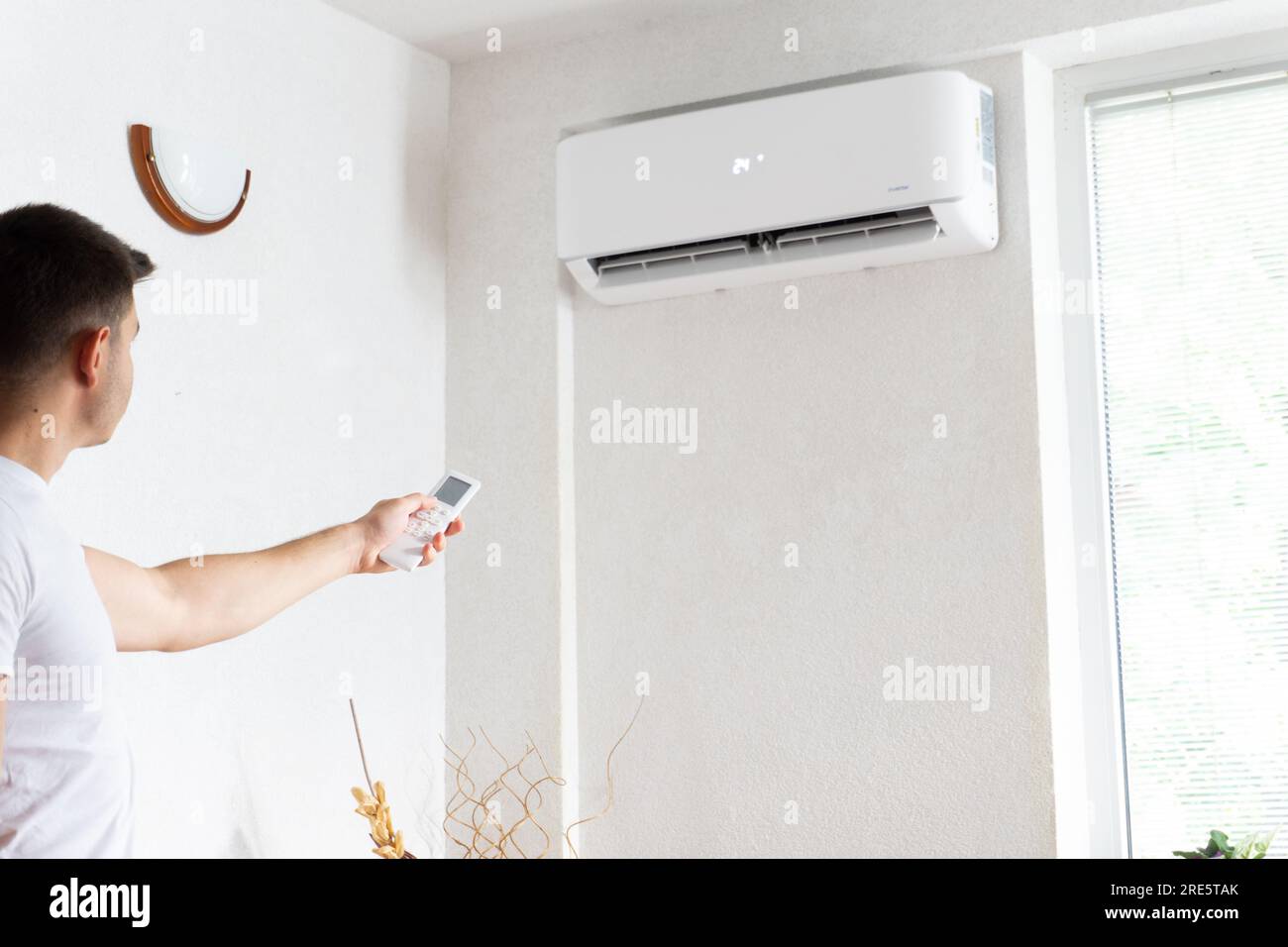 Young man switches air conditioning on. Handsome young man turning on ...