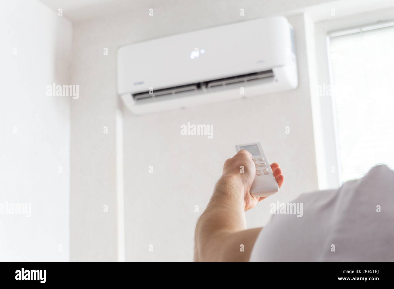 Hand holding remote control aimed at the air conditioner. Young man ...