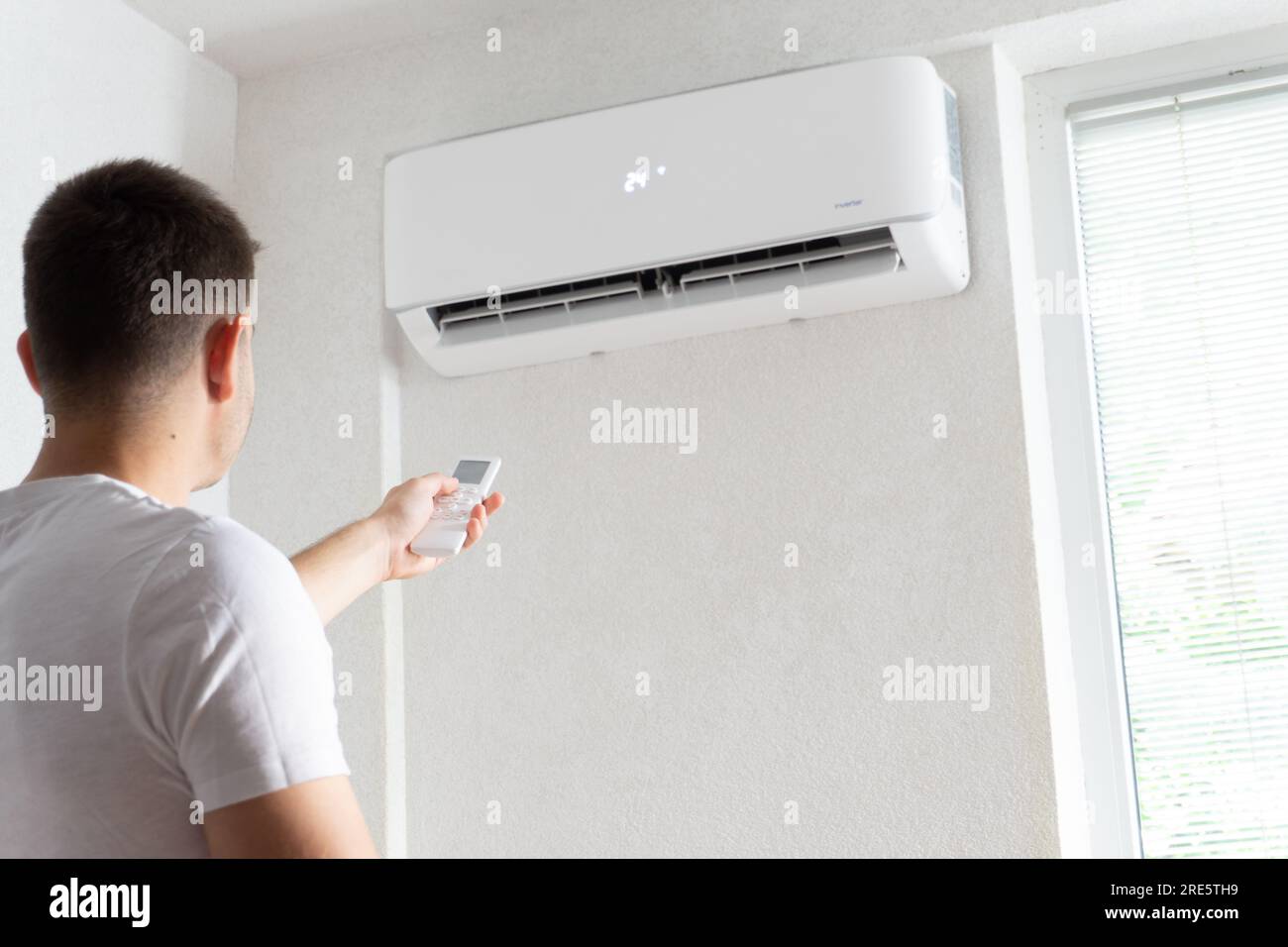 Young man switches air conditioning on. Handsome young man turning on ...