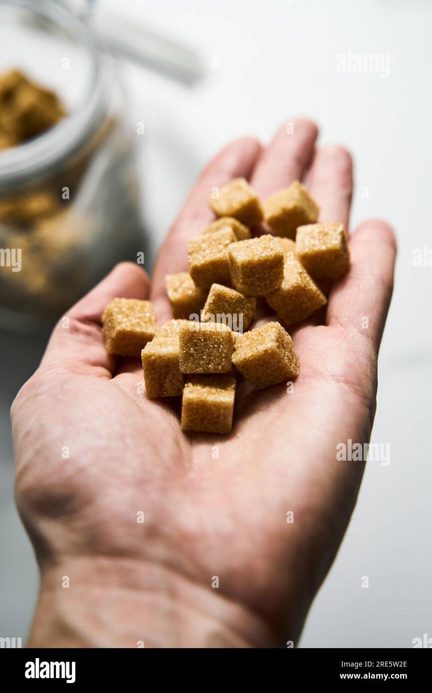 Brown sugar cubes in a man's hand and in the jar on white marble ...