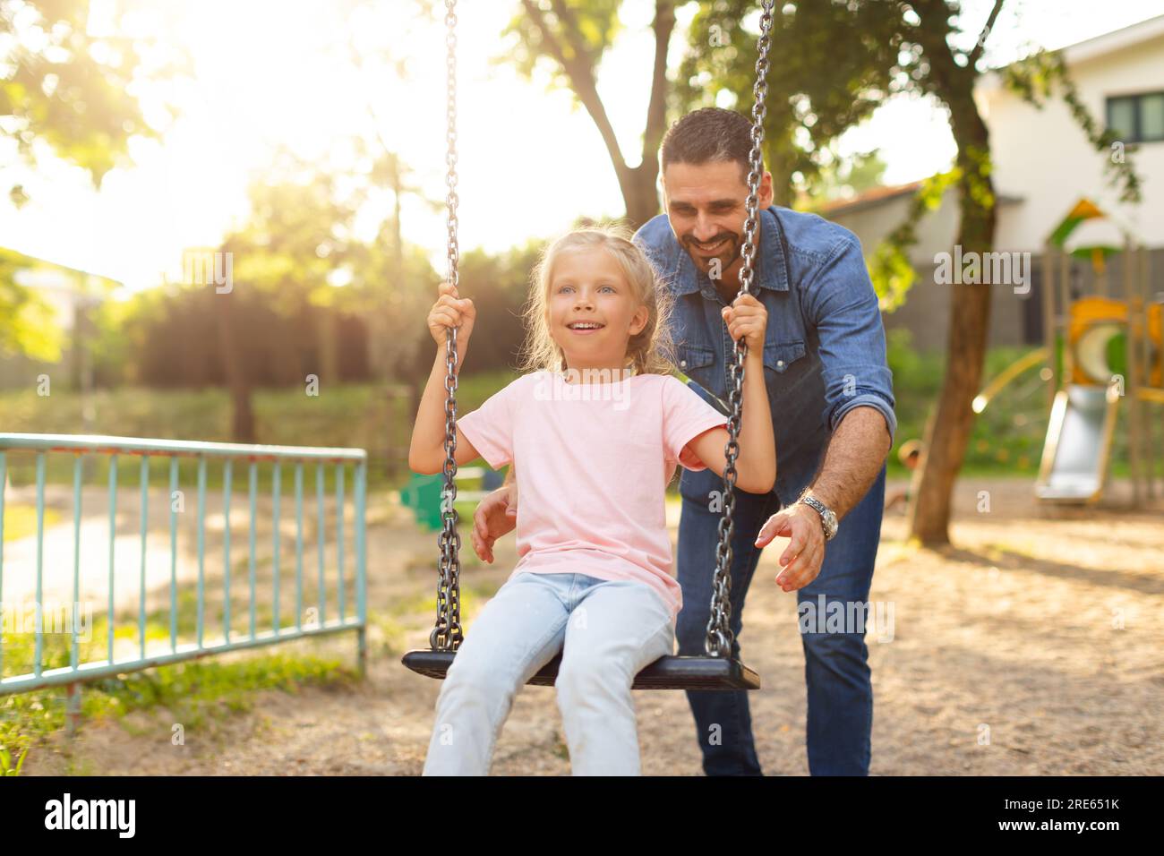 Park adventures. Happy middle aged father playing with his daughter on playground with swings ...