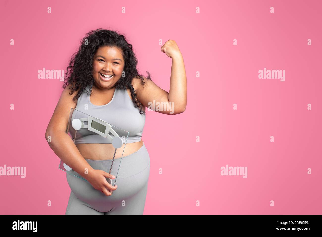 Positive black obese woman in sportswear holding scales and showing ...