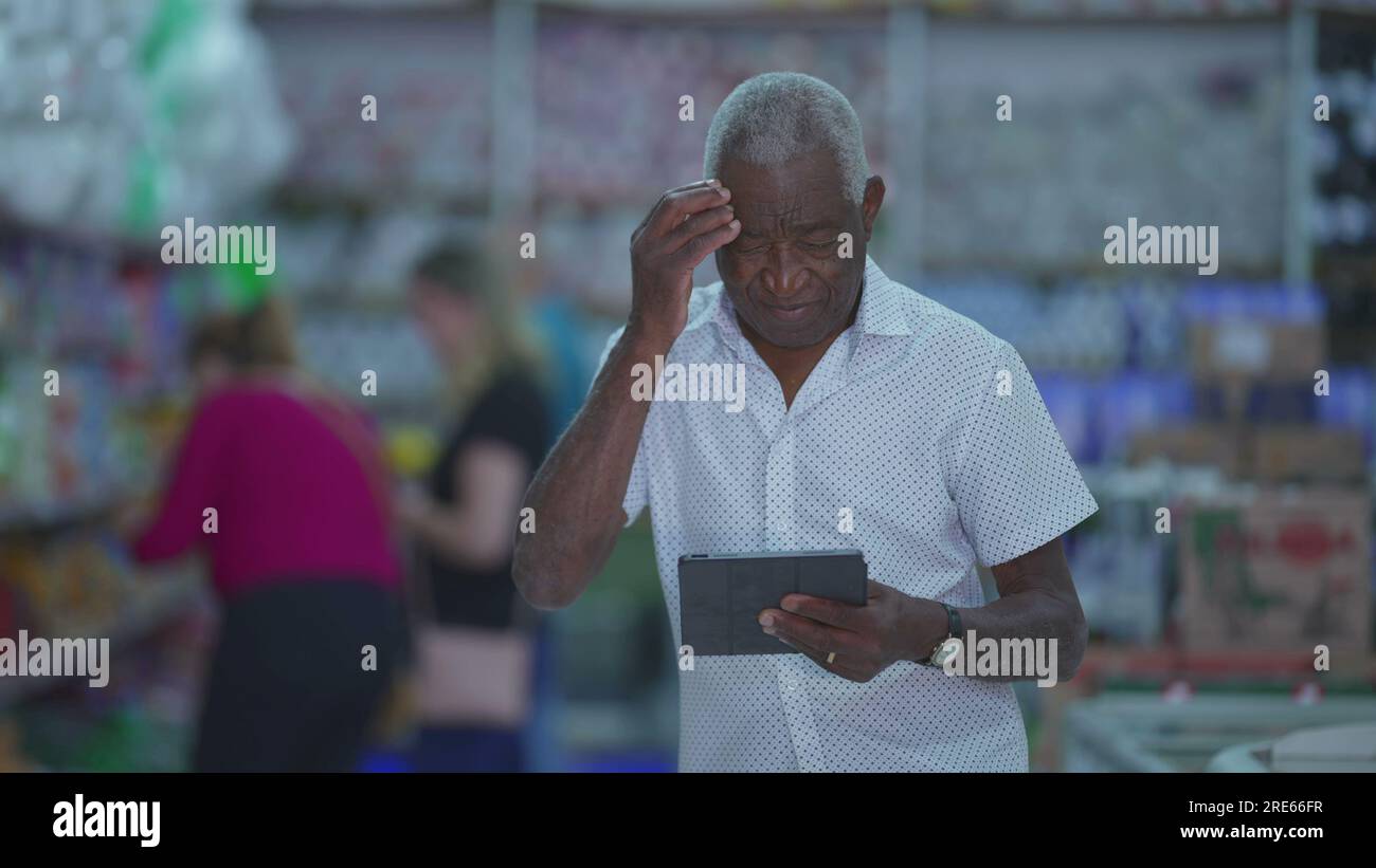 Confused senior man using tablet device inside small business store ...