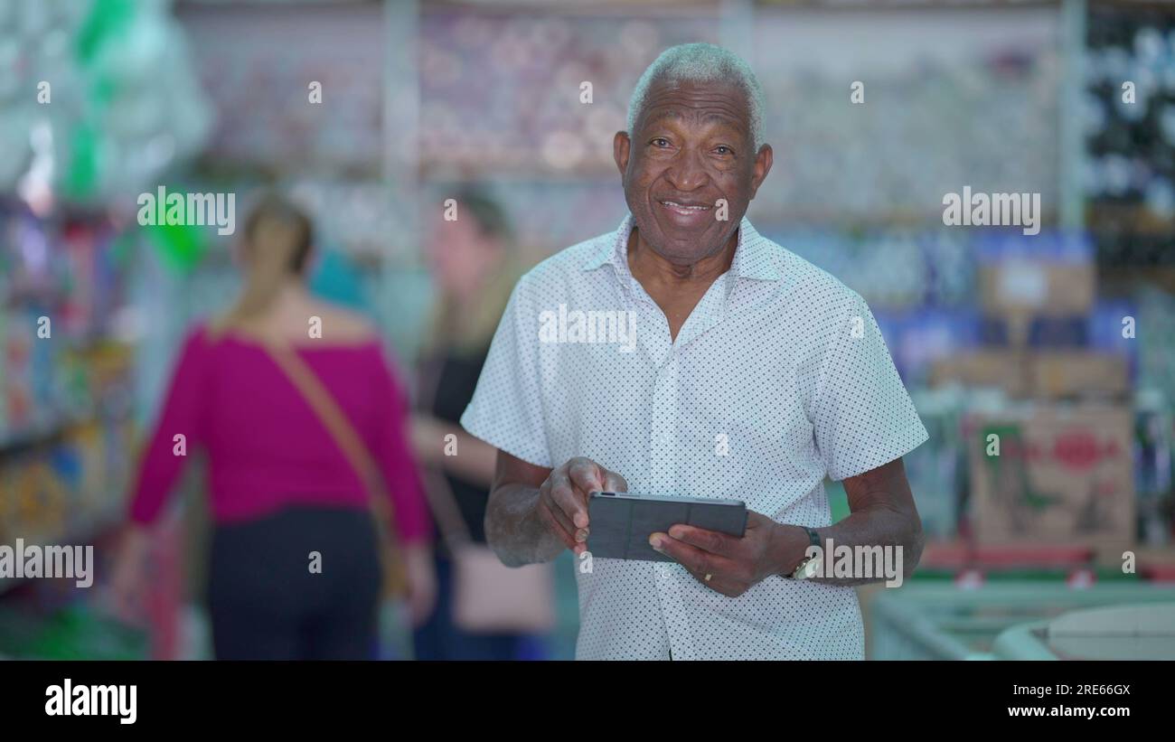One black senior Brazilian manager of grocery store holding tablet ...