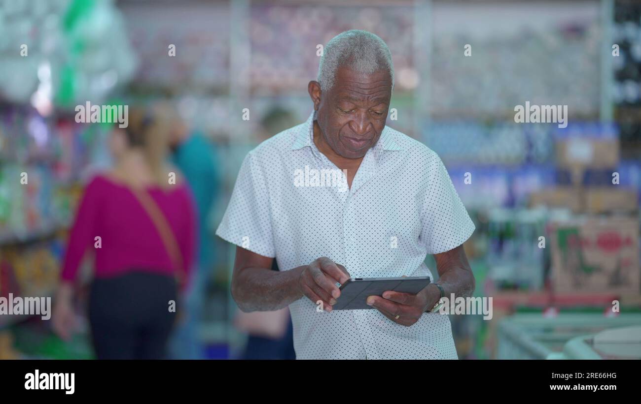 One black senior Brazilian manager of grocery store holding tablet ...